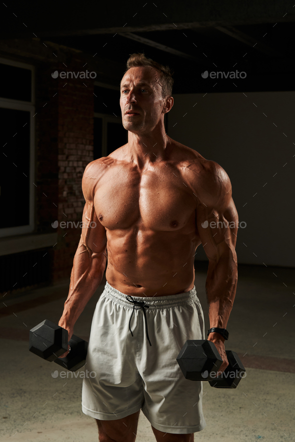The man with strong arms is exercising with shiny dumbbells. His torso ...