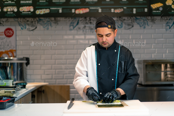 A sushi chef prepares maki rolls using nori avocado rice and bamboo mat ...