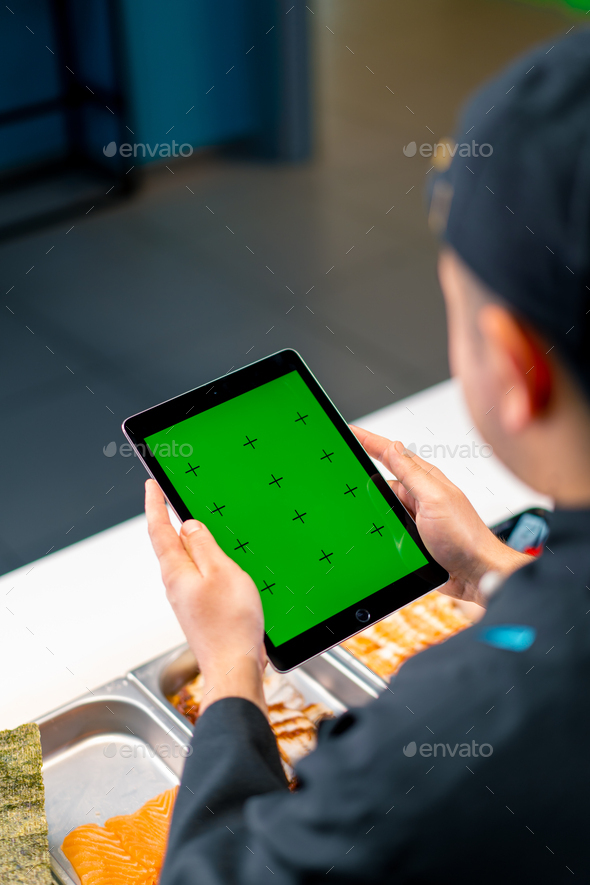 Close-up from behind the sushi chef holding a tablet with a green ...