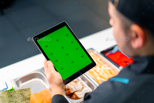 Close-up from behind the sushi chef holding a tablet with a green ...