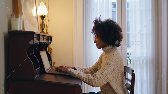 Focused model typing laptop keyboard at home. African woman working ...