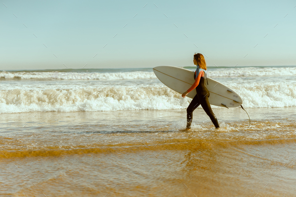 Side view of female surfer in wetsuit with his surfboard entering the ...