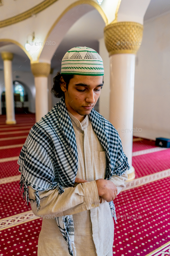 A young Muslim man in national Arabic clothing prays in a mosque during ...