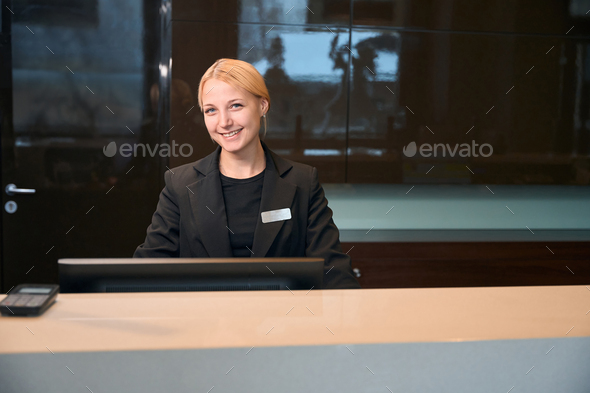 Young smiling european female receptionist at reception desk in hotel ...