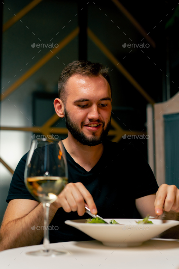 Close-up of a young guy with a beard eating salad in an Italian ...