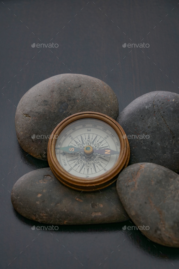 Antique brass compass laying on top of rocks. Stock Photo by wirestock