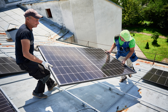 Workers building solar panel system on roof of house. Installers ...