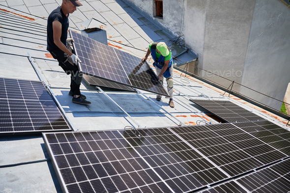 Workers building solar panel system on roof of house. Installers ...