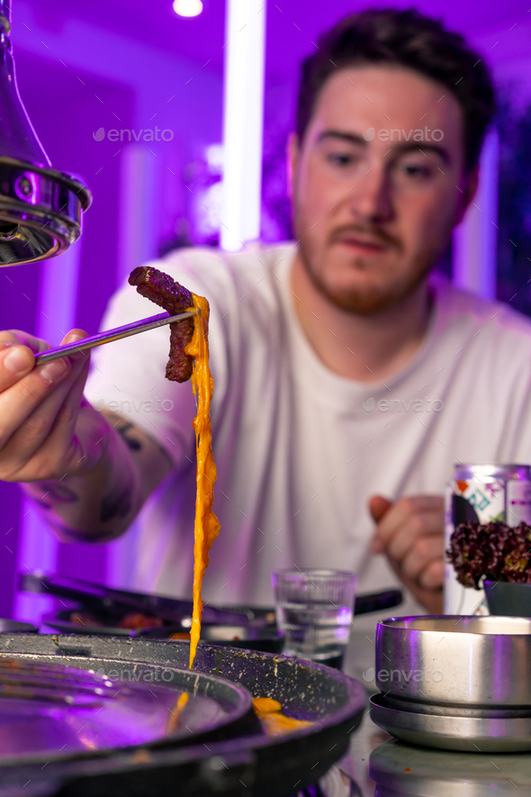 guests of restaurant take fried meat from the grill with chopsticks and ...