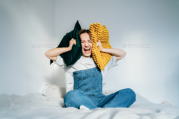 frustrated woman covers ears with pillows, screaming feels furious ...