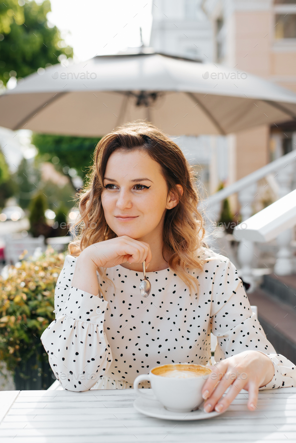 Stylish lady in dress and curly hairstyle having breakfast in street ...