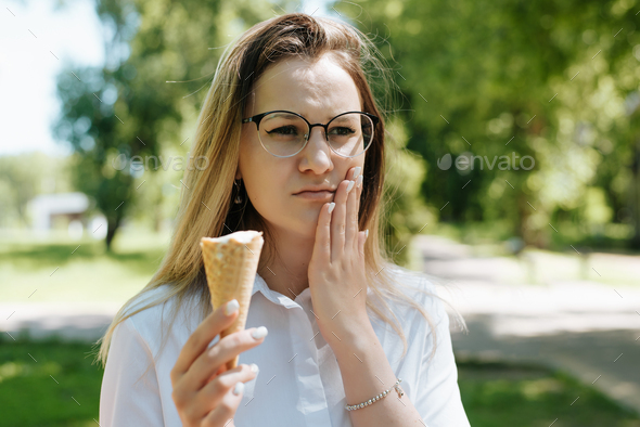 Young woman suffering from toothache and eating ice cream in waffle ...