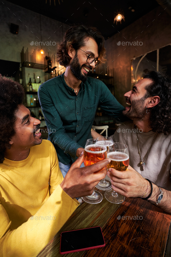 Group of three male friends gathered in a bar toasting with beers ...