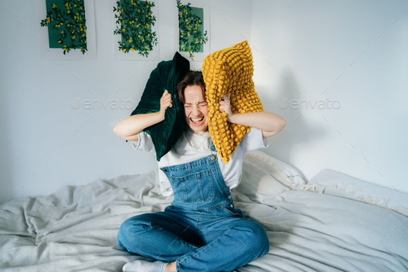 frustrated woman covers ears with pillows, screaming feels furious ...