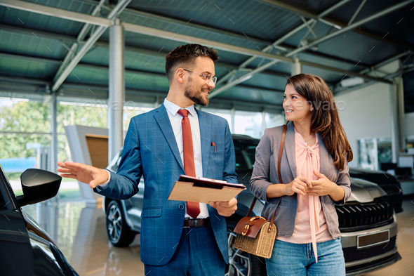 Happy salesman talking to female customer at car dealership. Stock ...