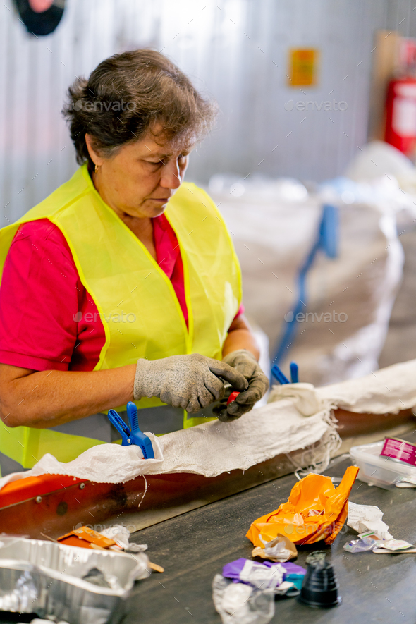 A serious older woman works at waste recycling station and sorts ...