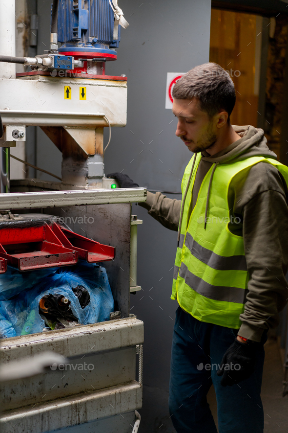 A recycling plant employee in uniform puts bags of garbage special ...