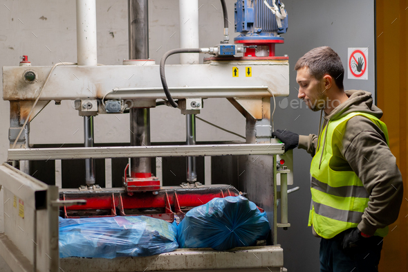 A recycling plant employee in uniform puts bags of garbage special ...