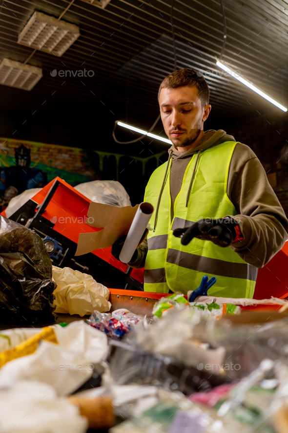 An employee in a uniform at a waste recycling station sorts and sorts ...