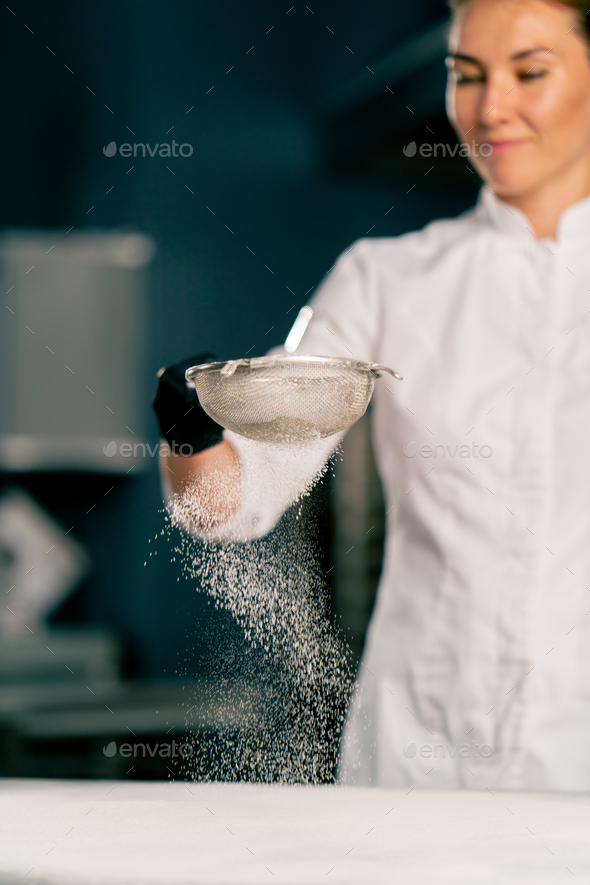 close-up shot of a female chef's hand sifting flour through a sieve ...