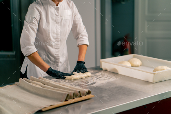 Concentrated female baker rolls dough into equal parts to create ...