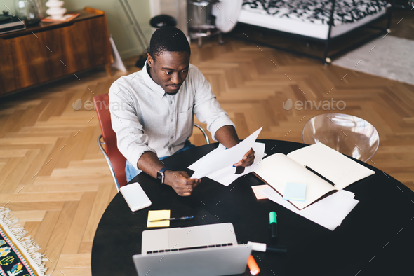 Focused black man reading documents in office Stock Photo by GaudiLab