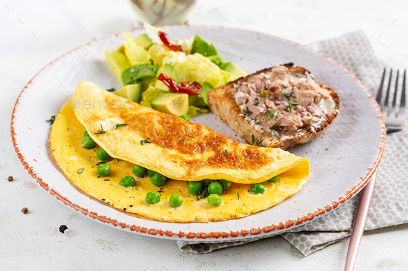 Omelette with green peas and toast with cod liver on white plate. Stock ...