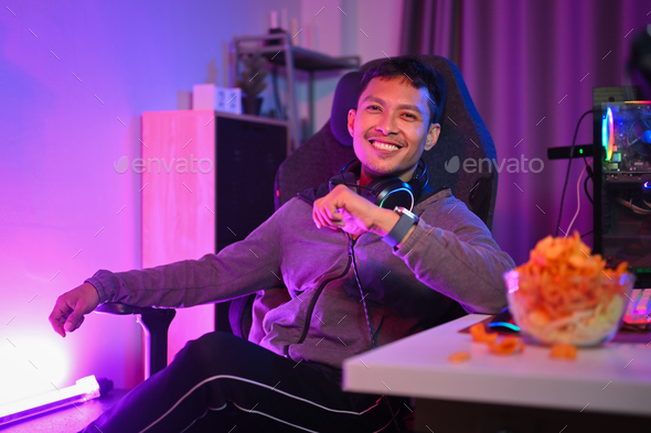 Smiling handsome man with headphone sitting on gaming chair in his room ...