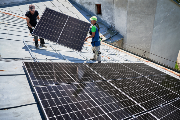 Workers building solar panel system on roof of house. Installers ...