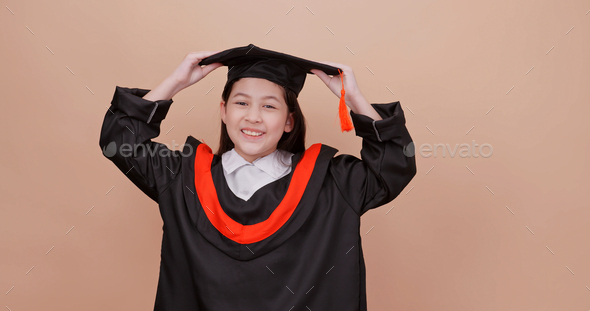 A school girl wearing a graduation gown makes happy gestures and ...