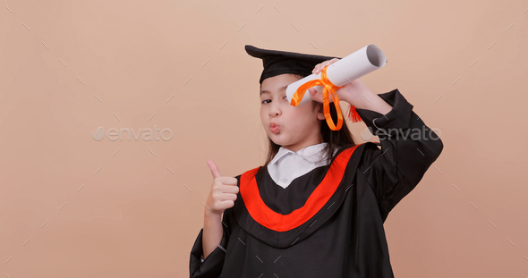 A school girl wearing a graduation gown makes happy gestures and ...