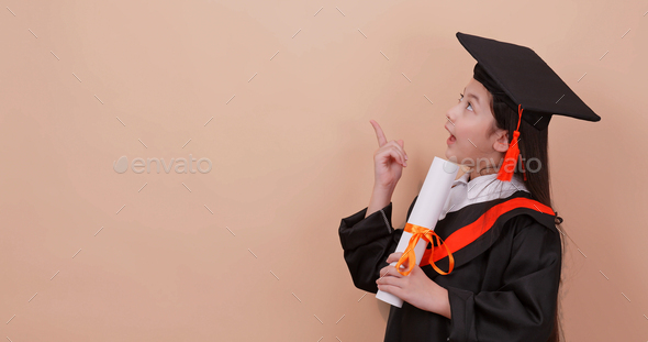 A school girl wearing a graduation gown makes happy gestures and ...