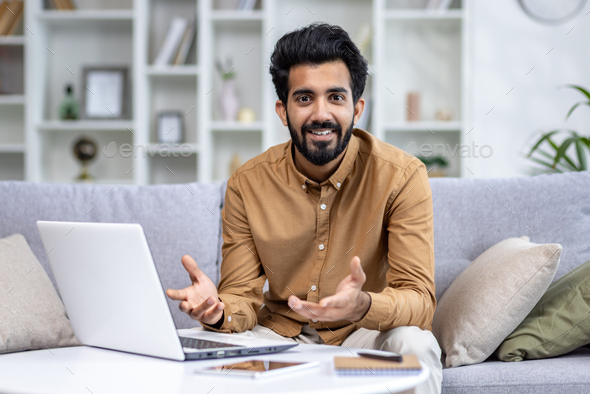 Smiling indian man talking during video call on laptop in apartment ...