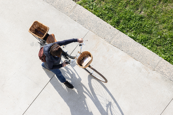 Woman walking with her bicycle equipped with baskets to carry objects ...