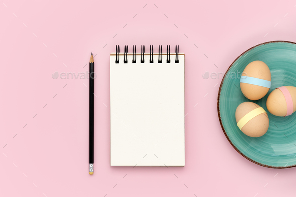 Blank notebook and pencil on pink background with plate and Easter eggs ...
