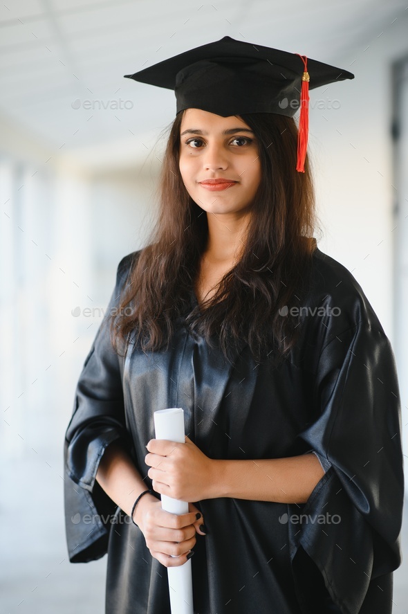 Happy Indian university student in graduation gown and cap holding ...