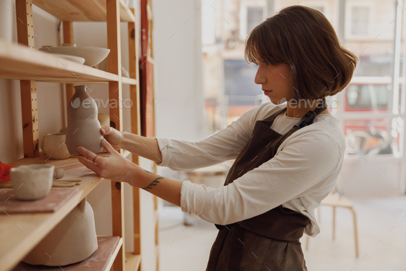Professional potter wearing apron holding unfired clay vase while ...