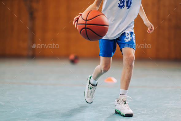 Cropped picture of junior basketball player in action dribbling a ball ...