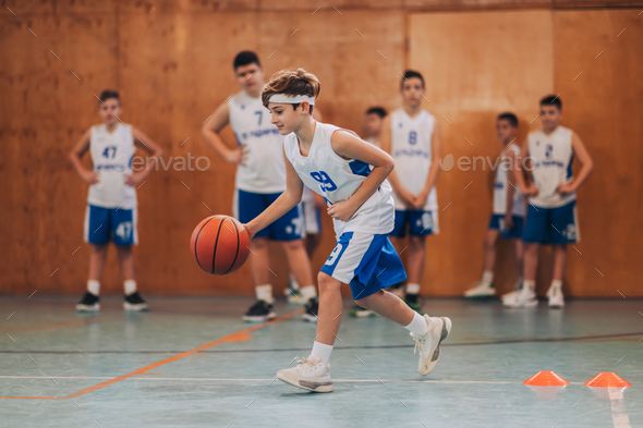 A junior basketball player dribbling a ball and practicing on court ...