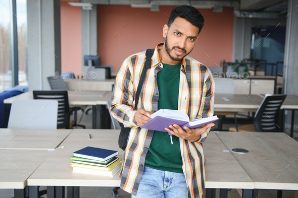 Young indian student boy reading book studying in college library with ...