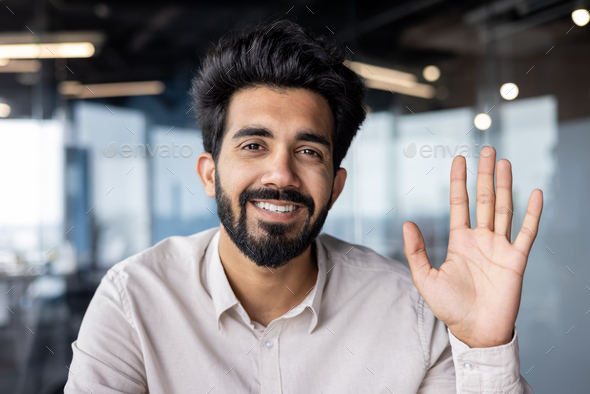 Cheerful indian businessman waving hello in modern office space ...