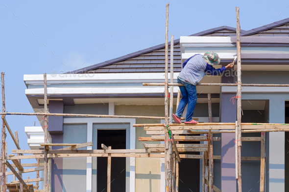 Painter on wooden scaffolding is painting roof eaves of modern house ...