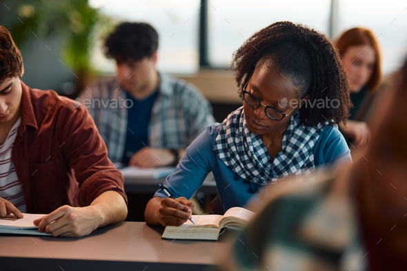 Black college student writing in her notebook while studying in the ...