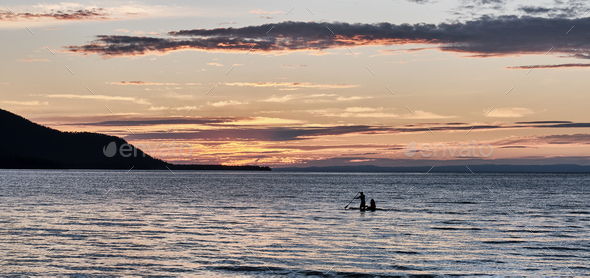 Barguzinsky Bay of Lake Baikal during colorful sunset, Russia. Silhouette of couple on SUP board ...