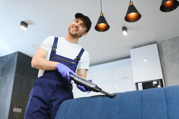 Cleaning service. Man janitor in gloves and uniform vacuum clean sofa ...