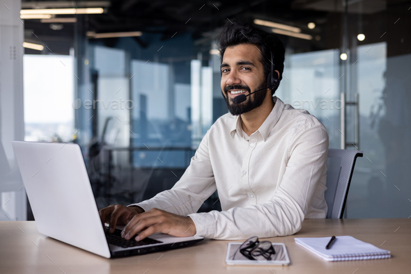 Smiling indian businessman in office setting with laptop and headset ...