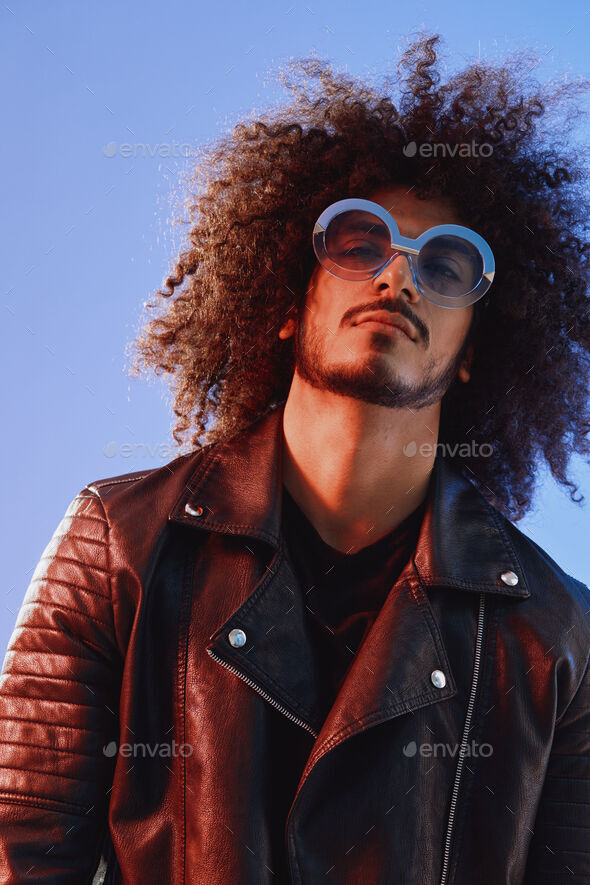 Portrait of a stylish man with curly hair with glasses smile on blue ...