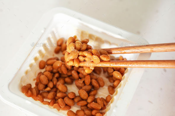Wooden chopsticks holding Japanese natto beans on white background top ...