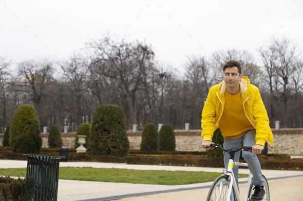happy caucasian young man riding a bicycle in a park si people in ...