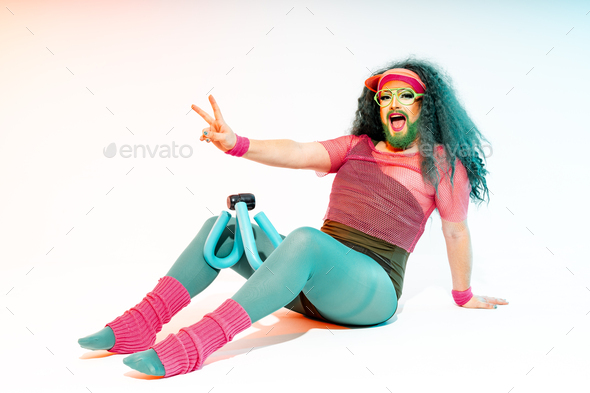 Smiling Drag Queen with long hair sitting on ground exercicing legs and ...